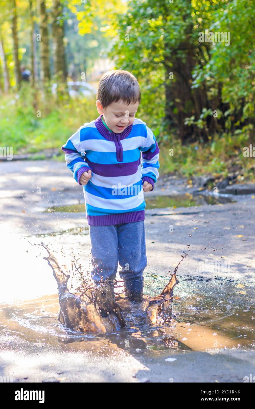 A little boy is jumping in a puddle. A boy in rubber boots. Happy ...