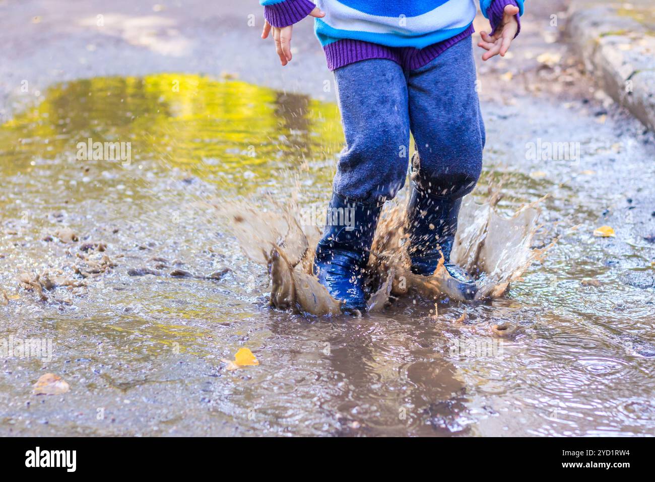A little boy is jumping in a puddle. A boy in rubber boots. Happy ...