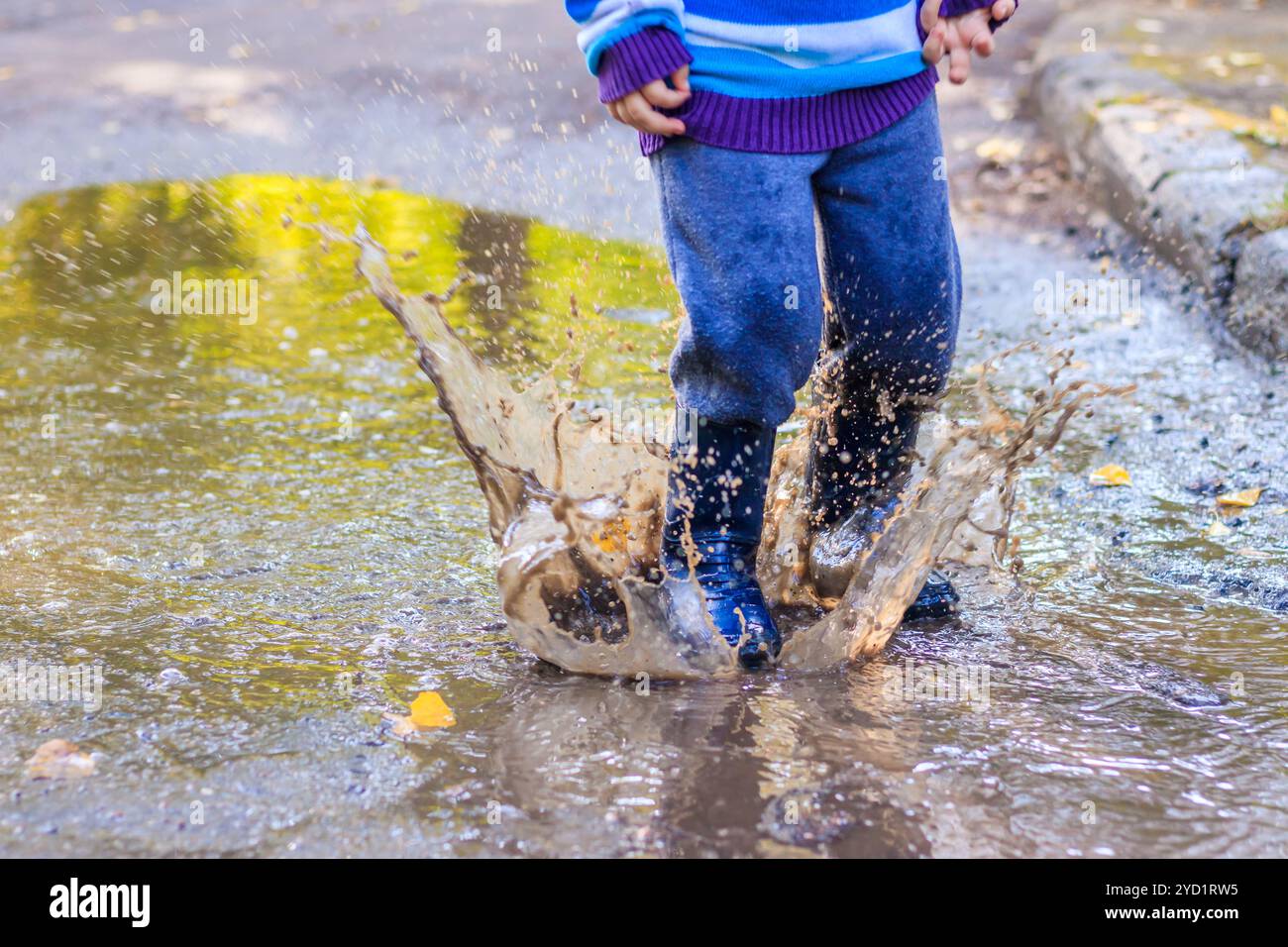 A little boy is jumping in a puddle. A boy in rubber boots. Happy ...