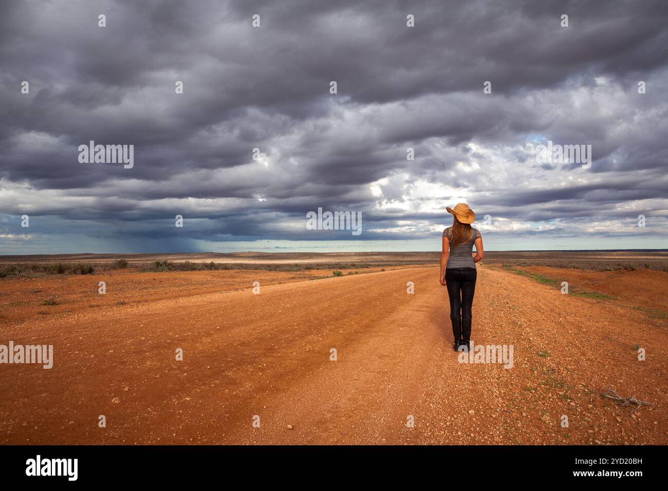 Farm girl watches the storm over an arid desert landscape of outback ...