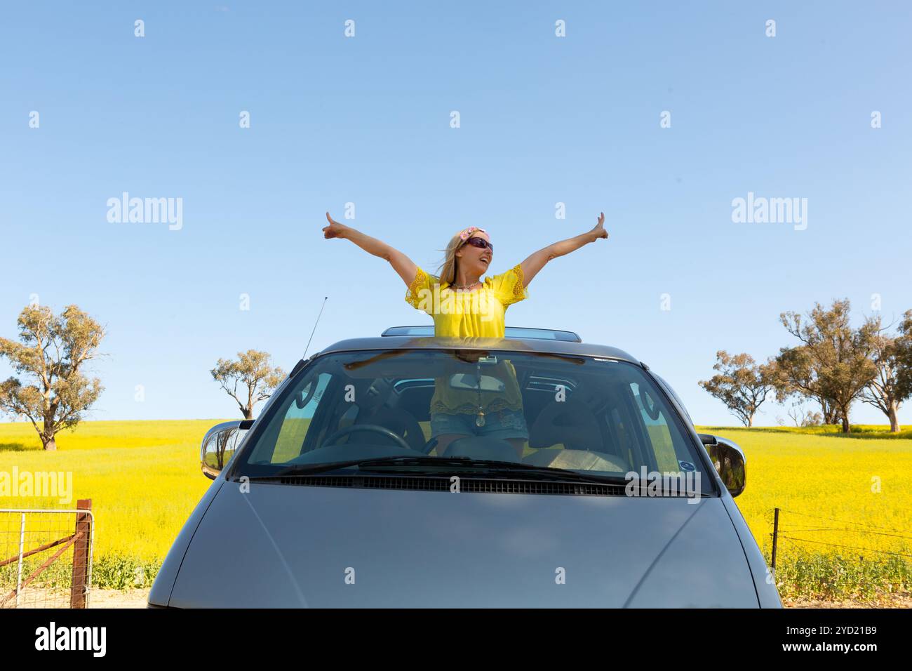 Happy woman standing out the sunroof of her 4wd car by canola field ...
