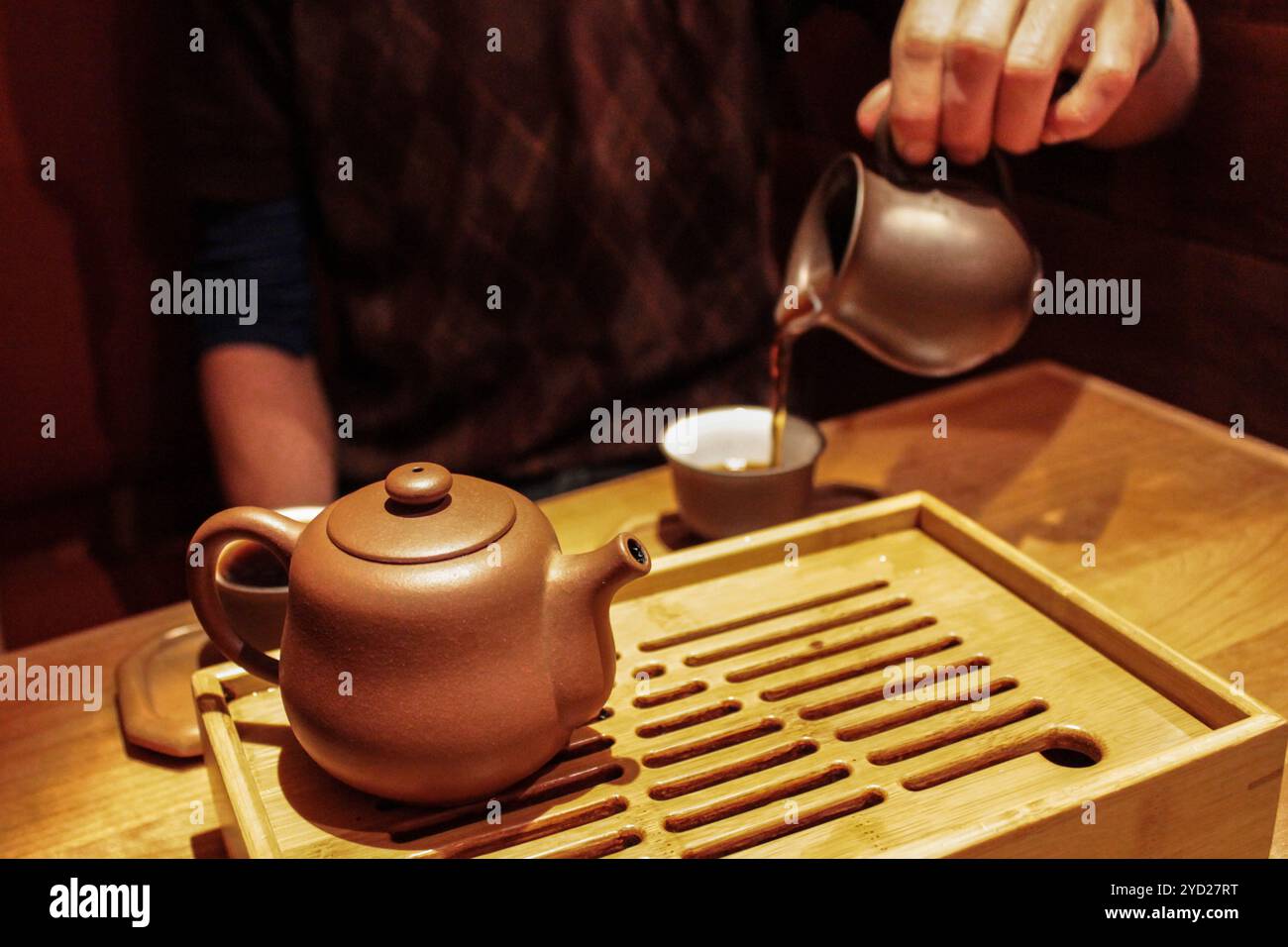 Pouring dark pu-erh tea from a purple clay jar into a small tasting cup ...