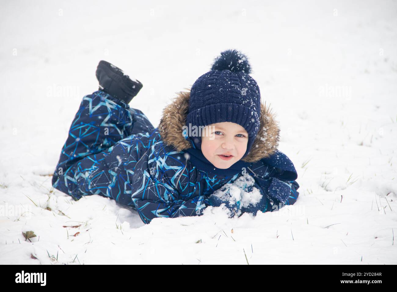 A little boy lies in the winter snow. Walk with the child. Winter walk ...