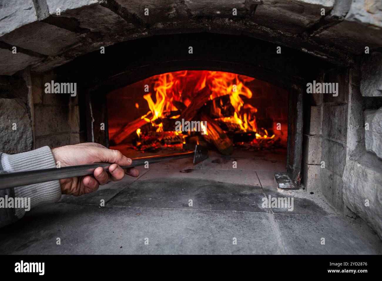 Bread oven with a fire inside, while man is moving wood around with a ...