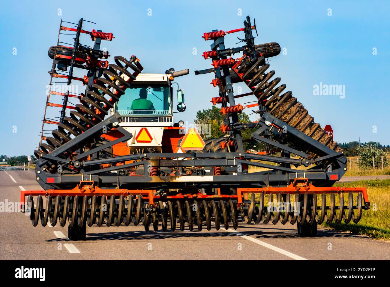 A farmer is seen driving a large industrial tractor from behind, with ...