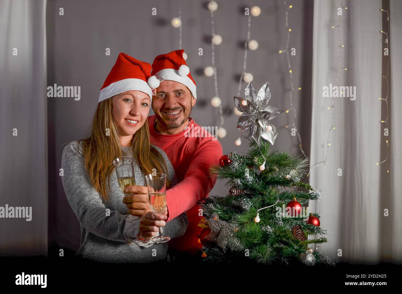 couple celebrating the beginning of Christmas, next to the tree, with 2 ...