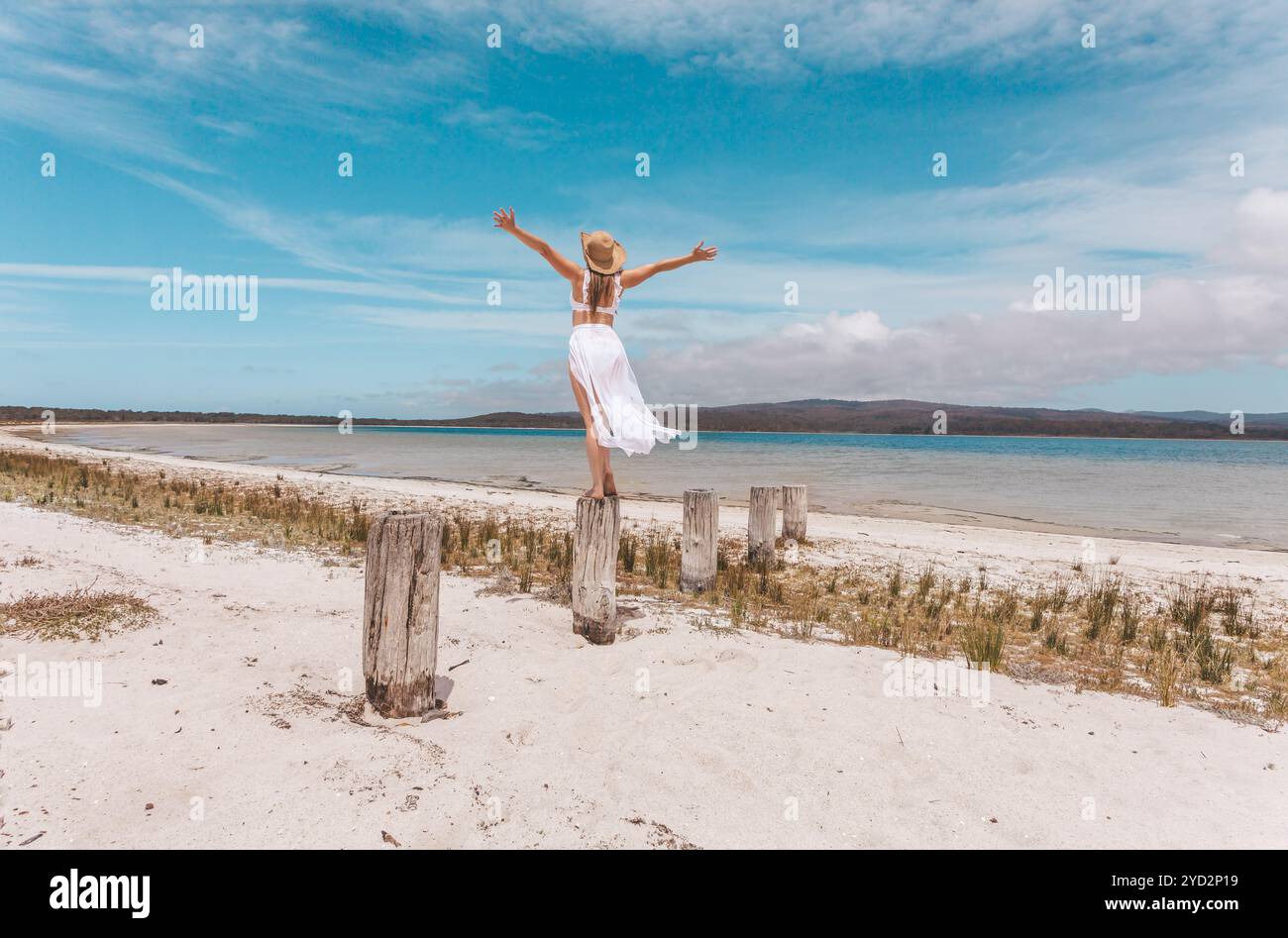 A female on vacation at the beach wearing a white swimsuit with sarong skirt,arms outstretched ...