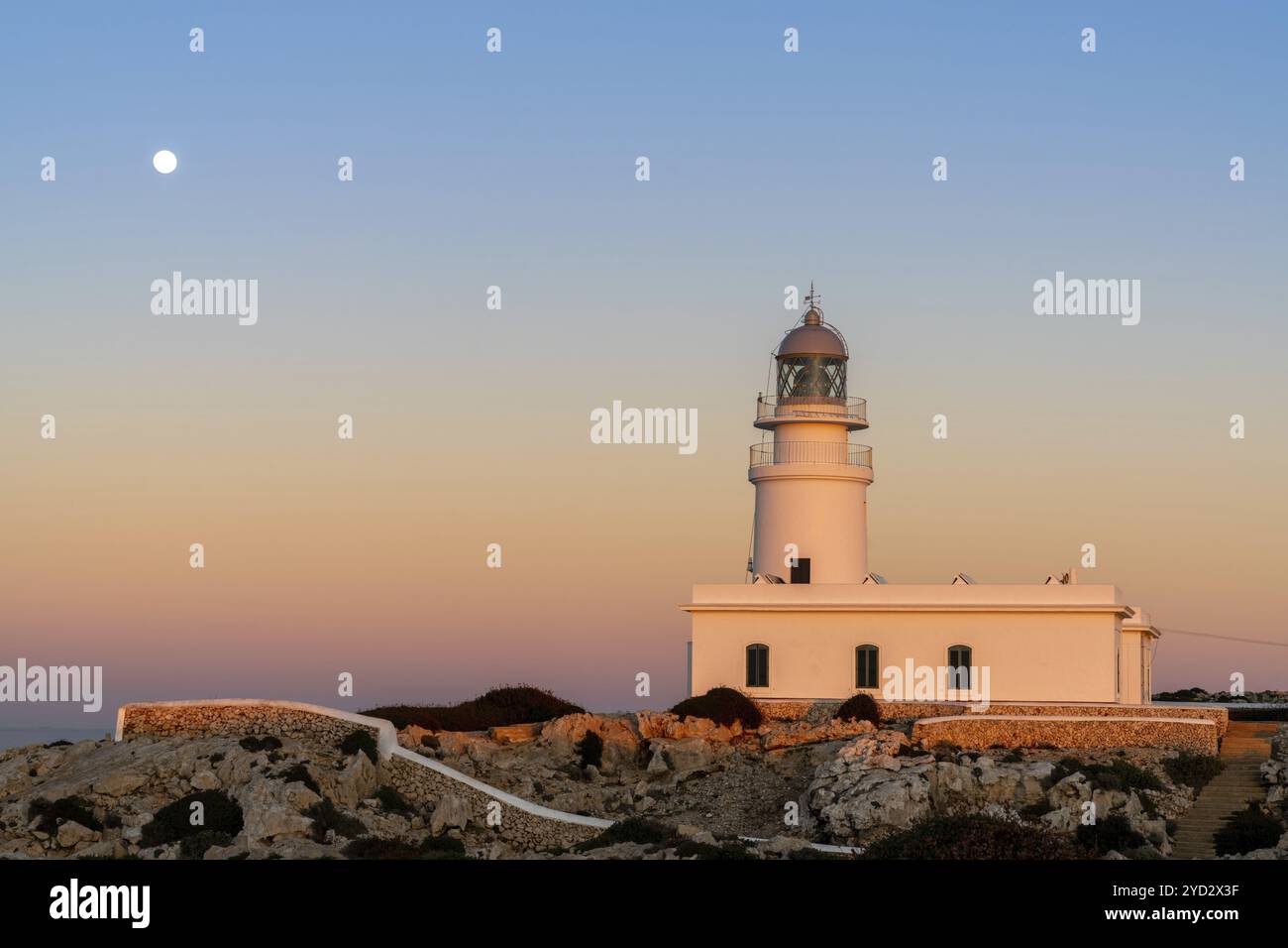 A vertical view of the Cap de Cavalleria Lighthouse on Menorca at sunset with a full moon rising ...