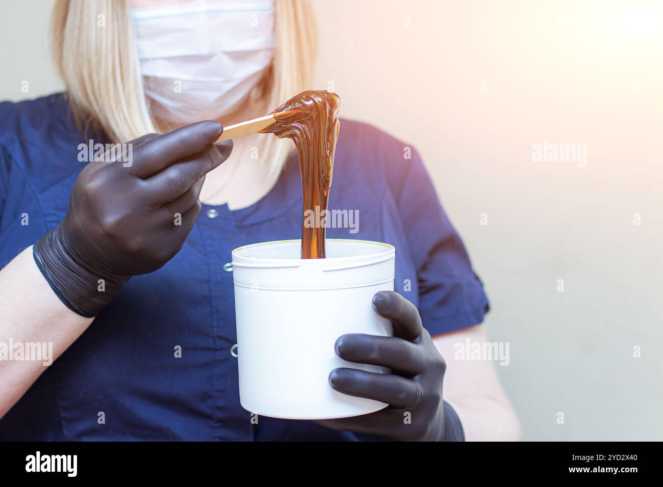 Female hands in black gloves holding a bowl of shugar paste ready for sugaring epilation ...