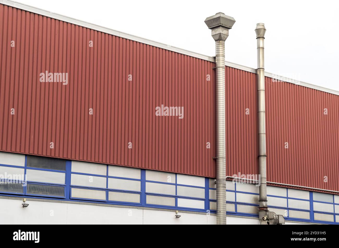 Red industrial building facade with metal pipes and windows on a cloudy ...