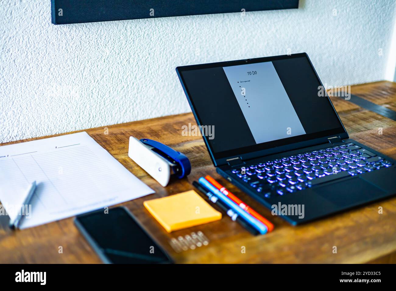 A laptop is open on a desk with a stack of papers and a pen. The laptop ...