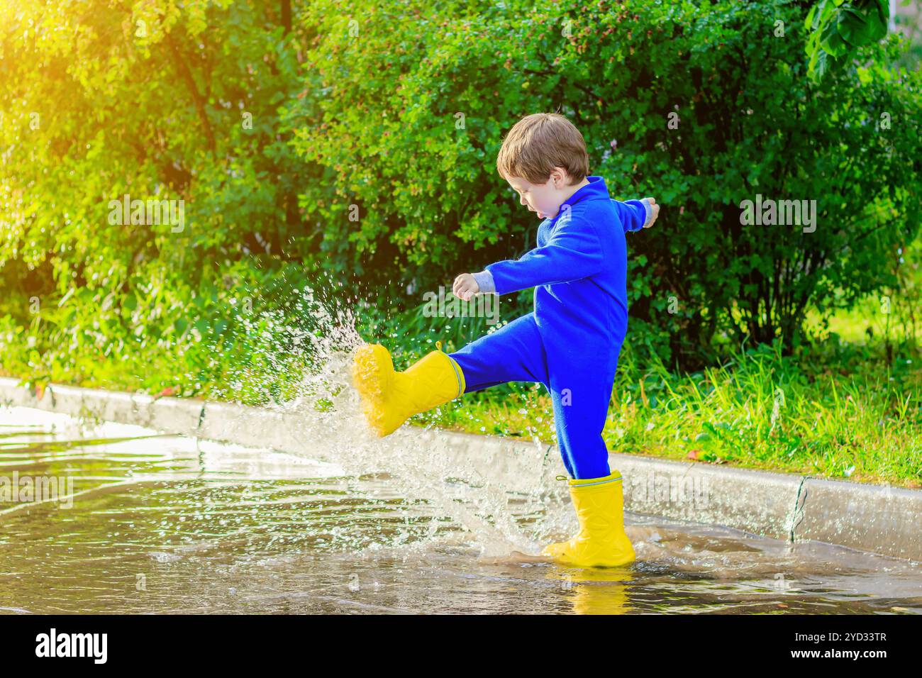 A happy boy in rubber boots jumps in puddles. The boy jumps in a puddle ...