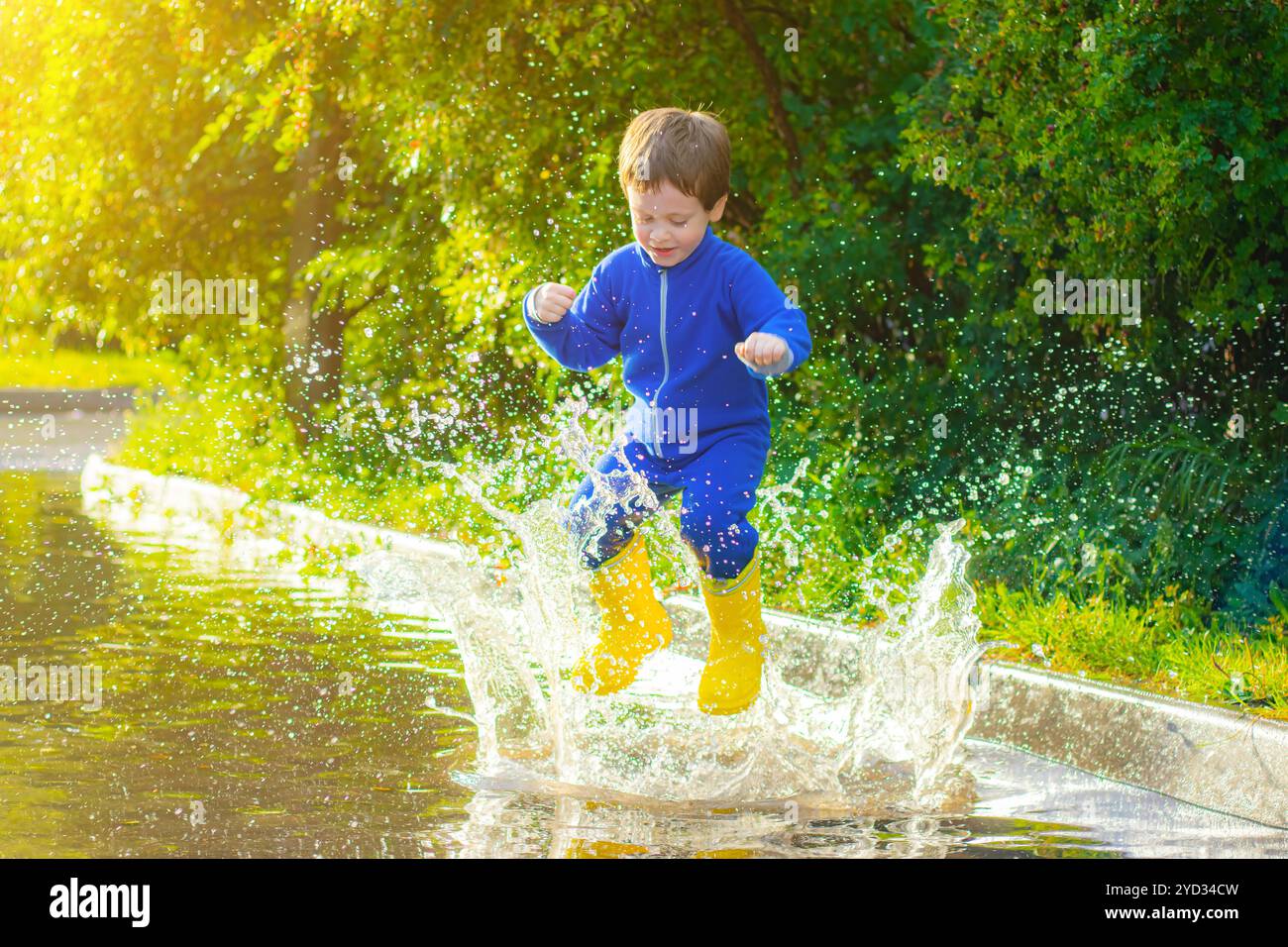 A happy boy in rubber boots jumps in puddles. The boy jumps in a puddle . Bad weather. puddles ...