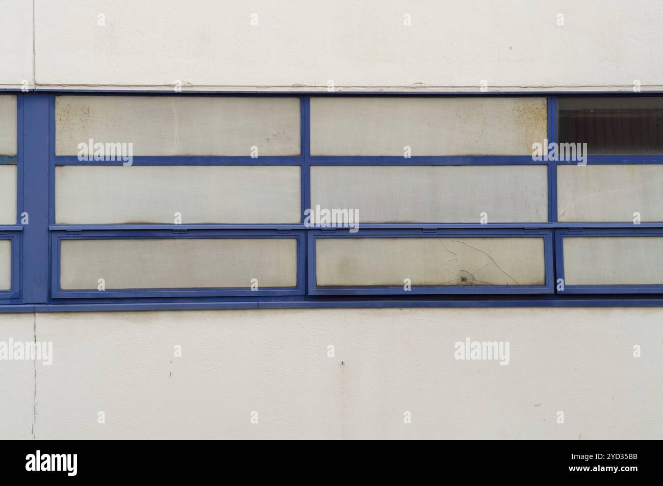 Old, dirty windows with blue frames are lined up against a white wall ...
