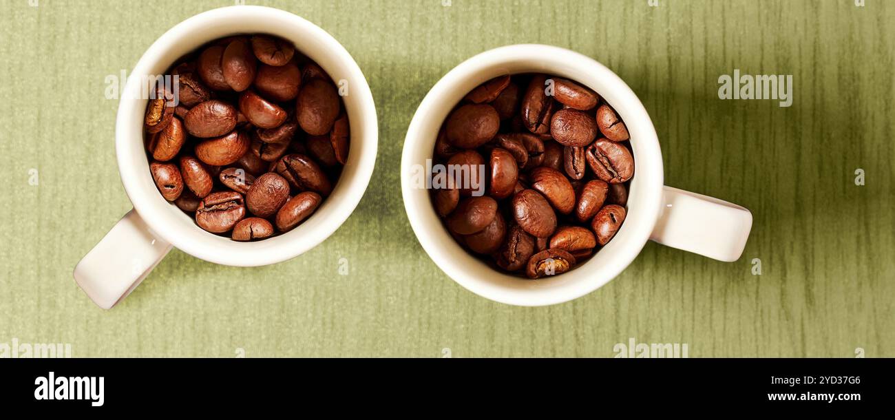 Two white cups filled with roasted coffee beans are placed on a green ...