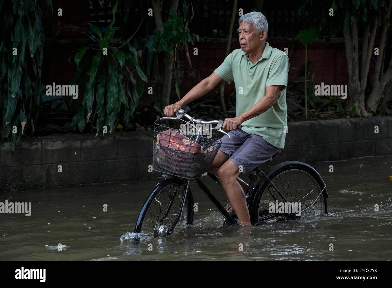 A resident rides his bike as he crosses flooded streets caused by ...