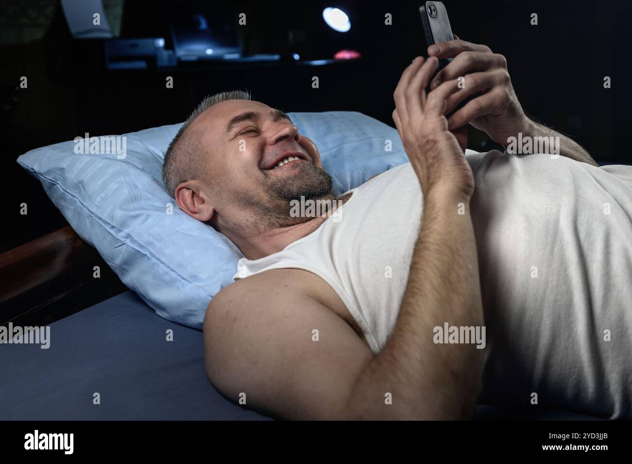 Man with smartphone in bed at night. Handsome man using mobile phone in ...