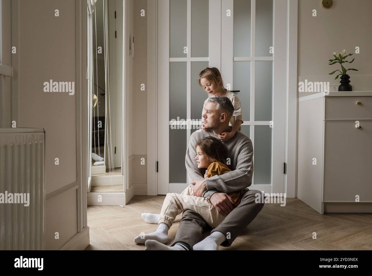 A father sits on the floor with his two daughters, surrounded by warmth ...