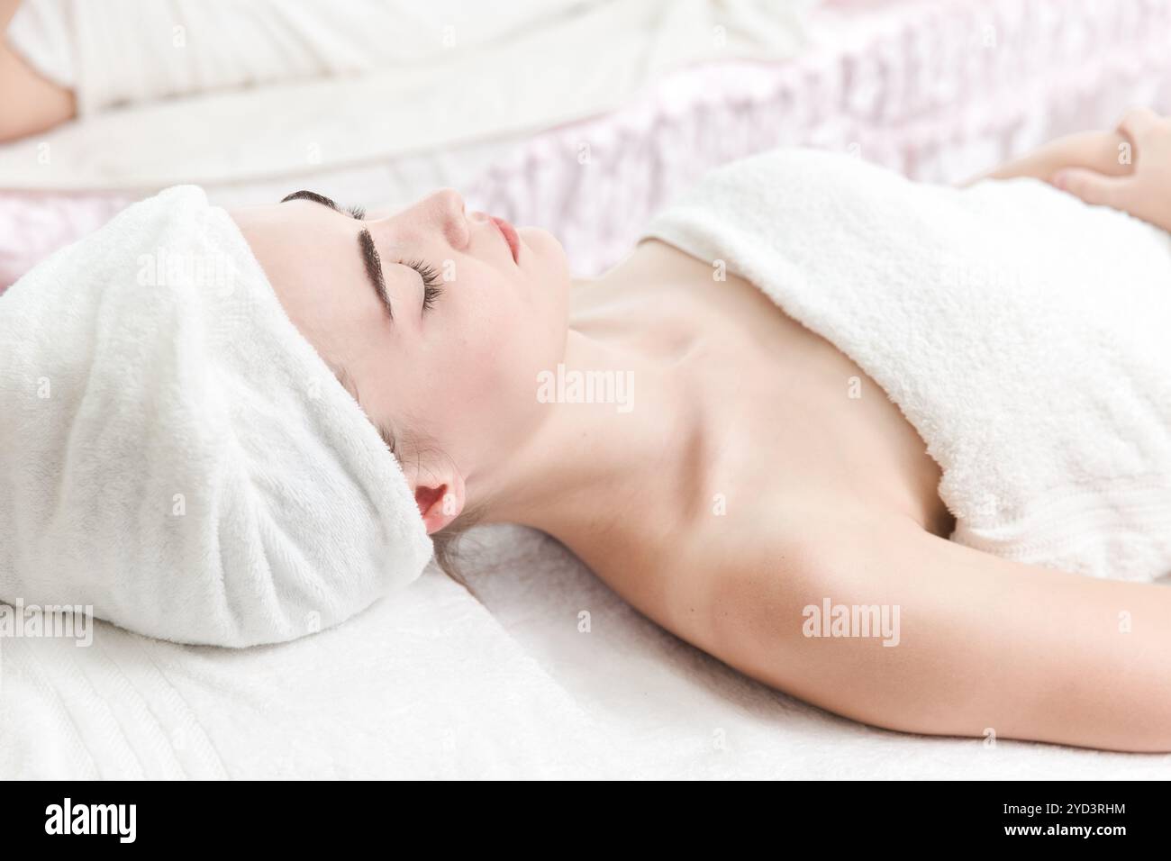 Young woman relaxing on a spa bed with a towel wrapped around her head, receiving a tranquil spa ...