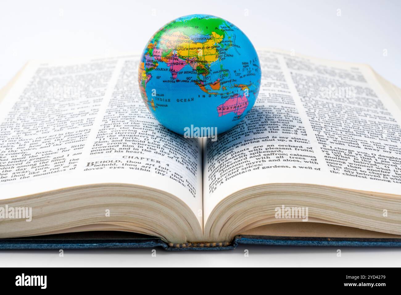 Opened book of Holy Bible with globe. It is laying on white background ...