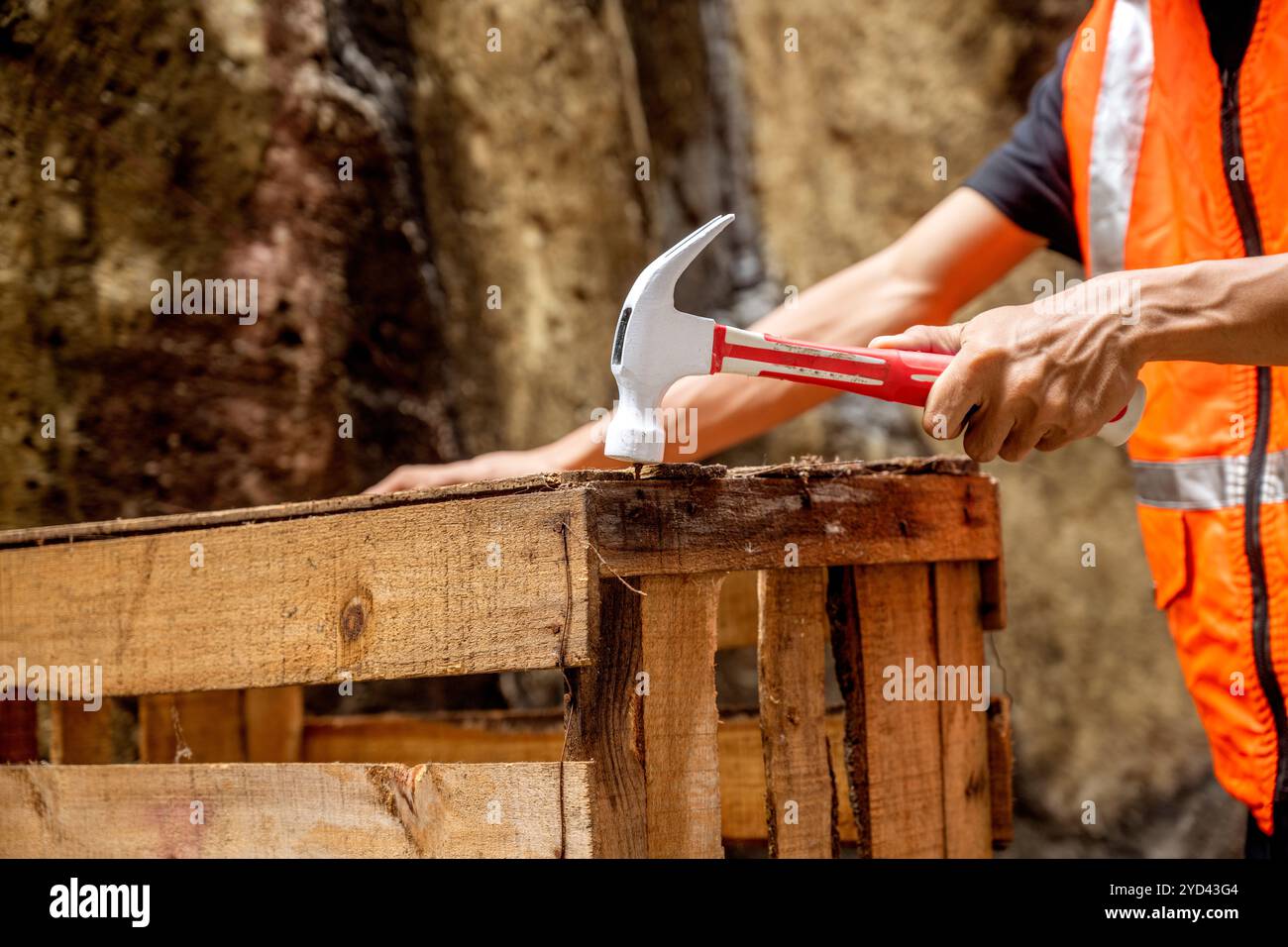 Workers in safety vest using hammer to to work assembling pallet parts ...