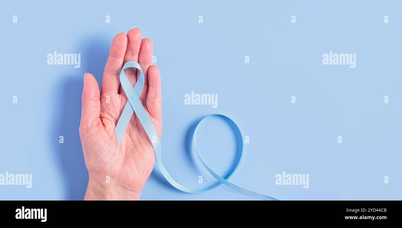 Blue cancer ribbon in womans hands on blue background Stock Photo - Alamy