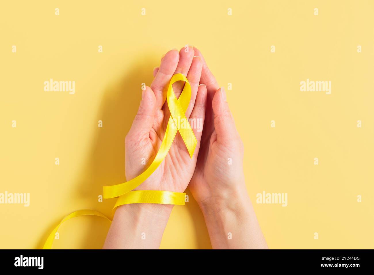 Yellow cancer ribbon in womens hands on yellow background Stock Photo ...