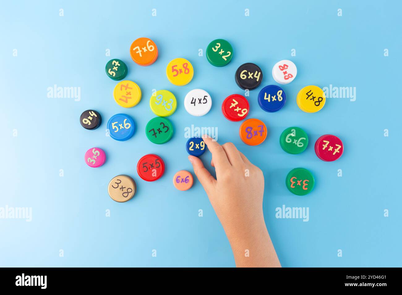 Child hands arranging colorful bottle caps with multiplication problems ...