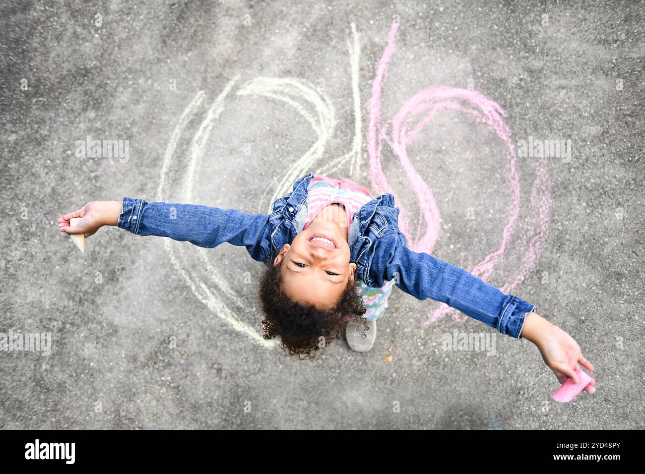 Smiling child holding chalk, arms outstretched, drawing on pavem Stock ...