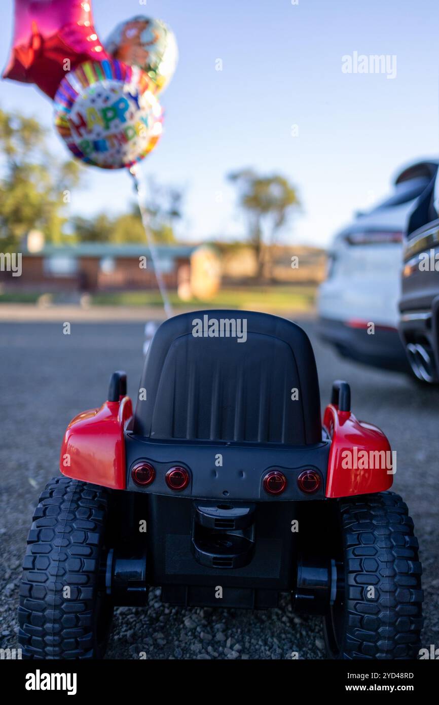 A small red toy car with birthday balloons tied to it, parked outdoors ...