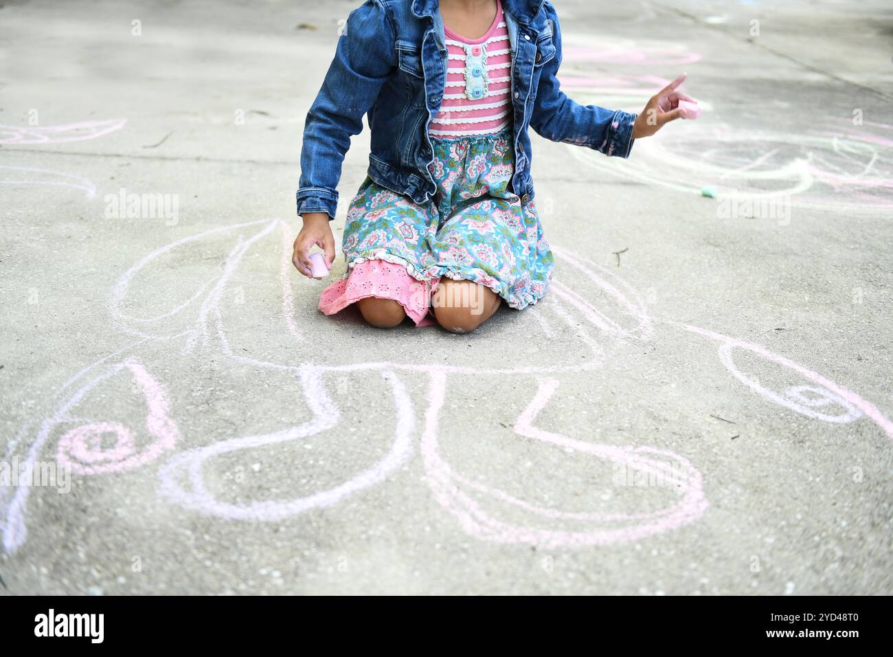 Child kneeling on pavement, drawing large chalk art with pastel Stock ...
