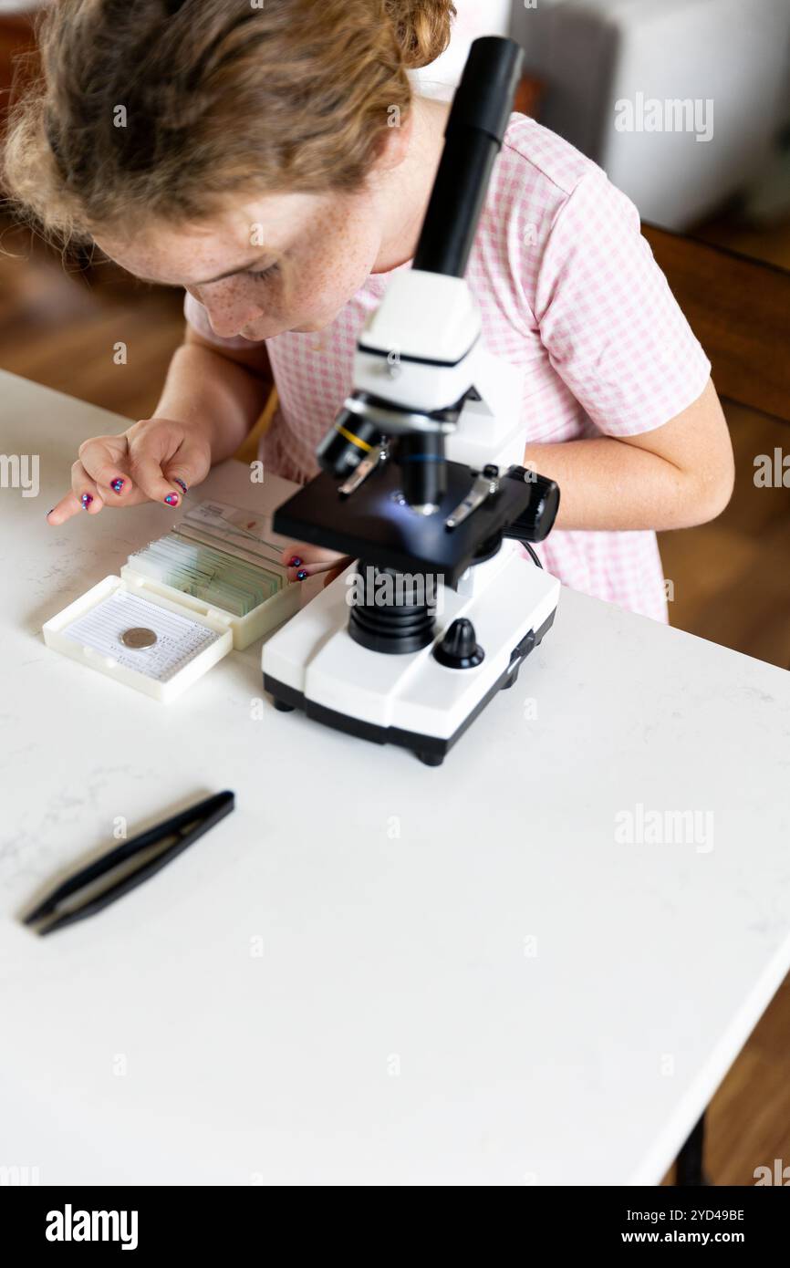 A girl with freckles examines microscope slides next to a microscope ...