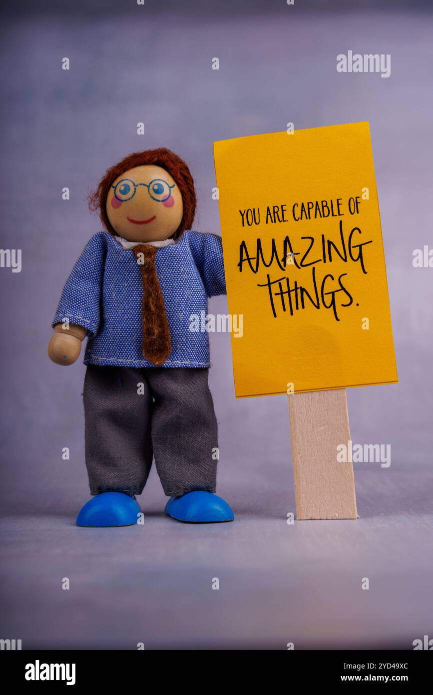 A toy man made of wood holds a yellow sign with a motivational phrase ...