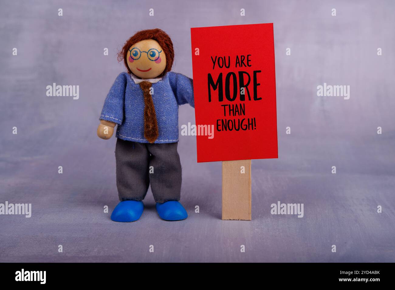 A wooden toy figure stands proudly with a red sign displaying a ...
