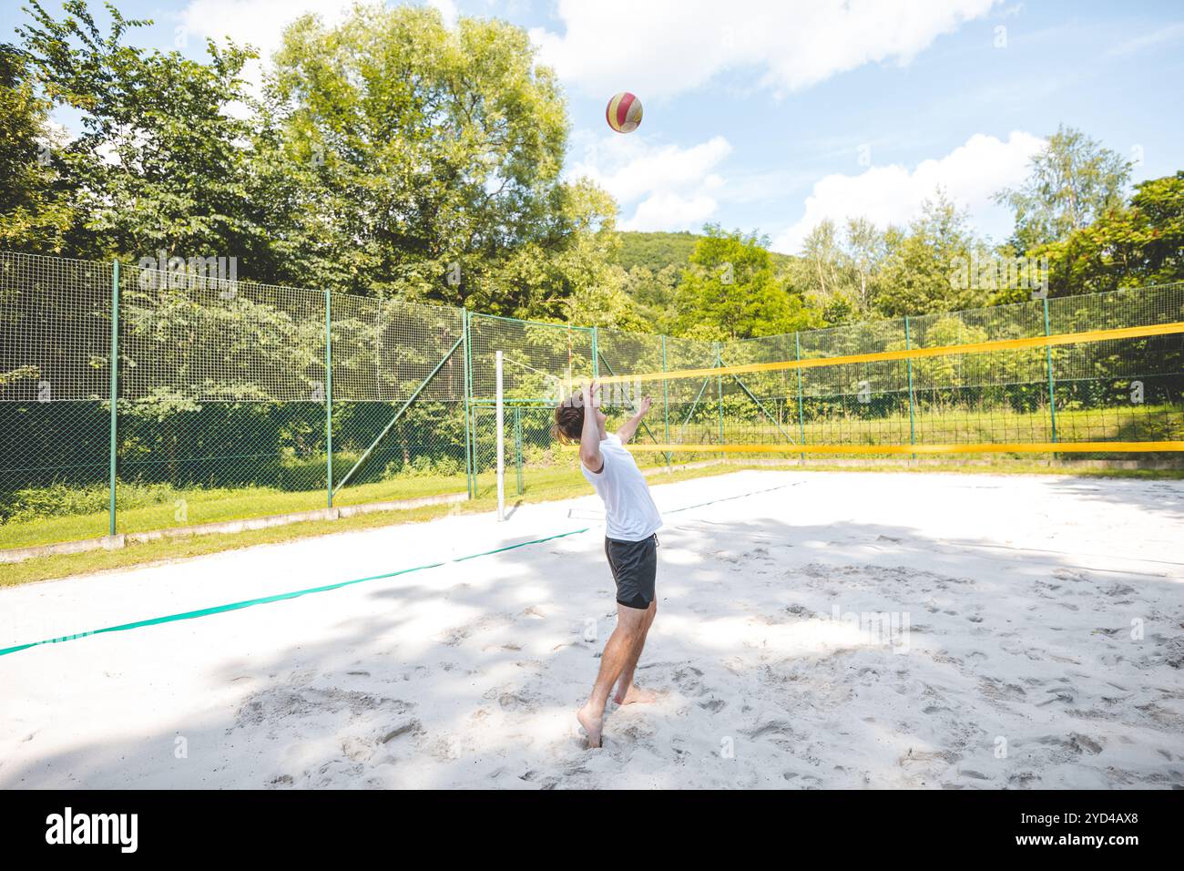 Volleyball player jumping to hit the ball over the net on a sand court ...