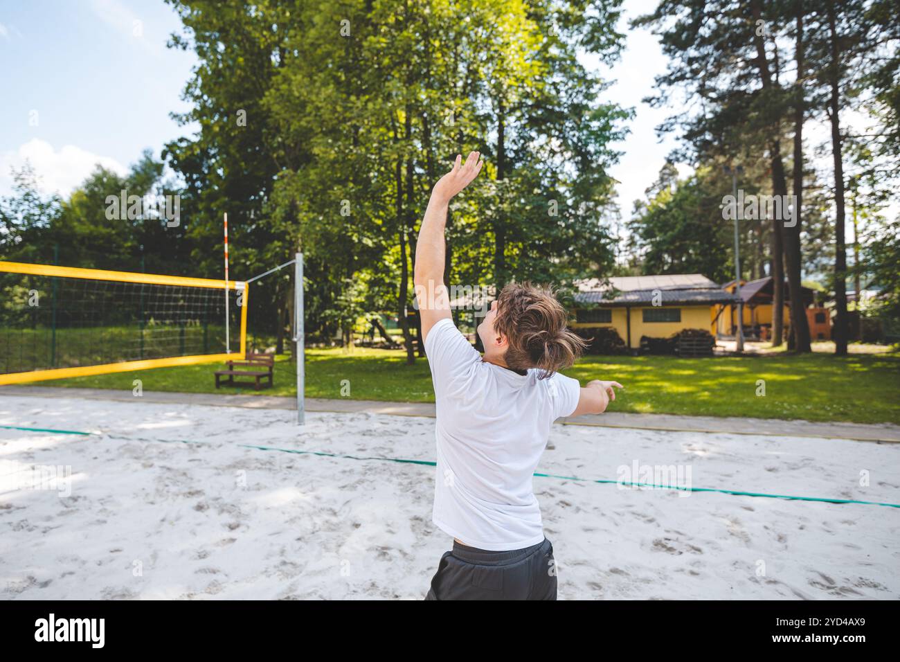 Volleyball player jumping to hit the ball over the net on a sand court ...