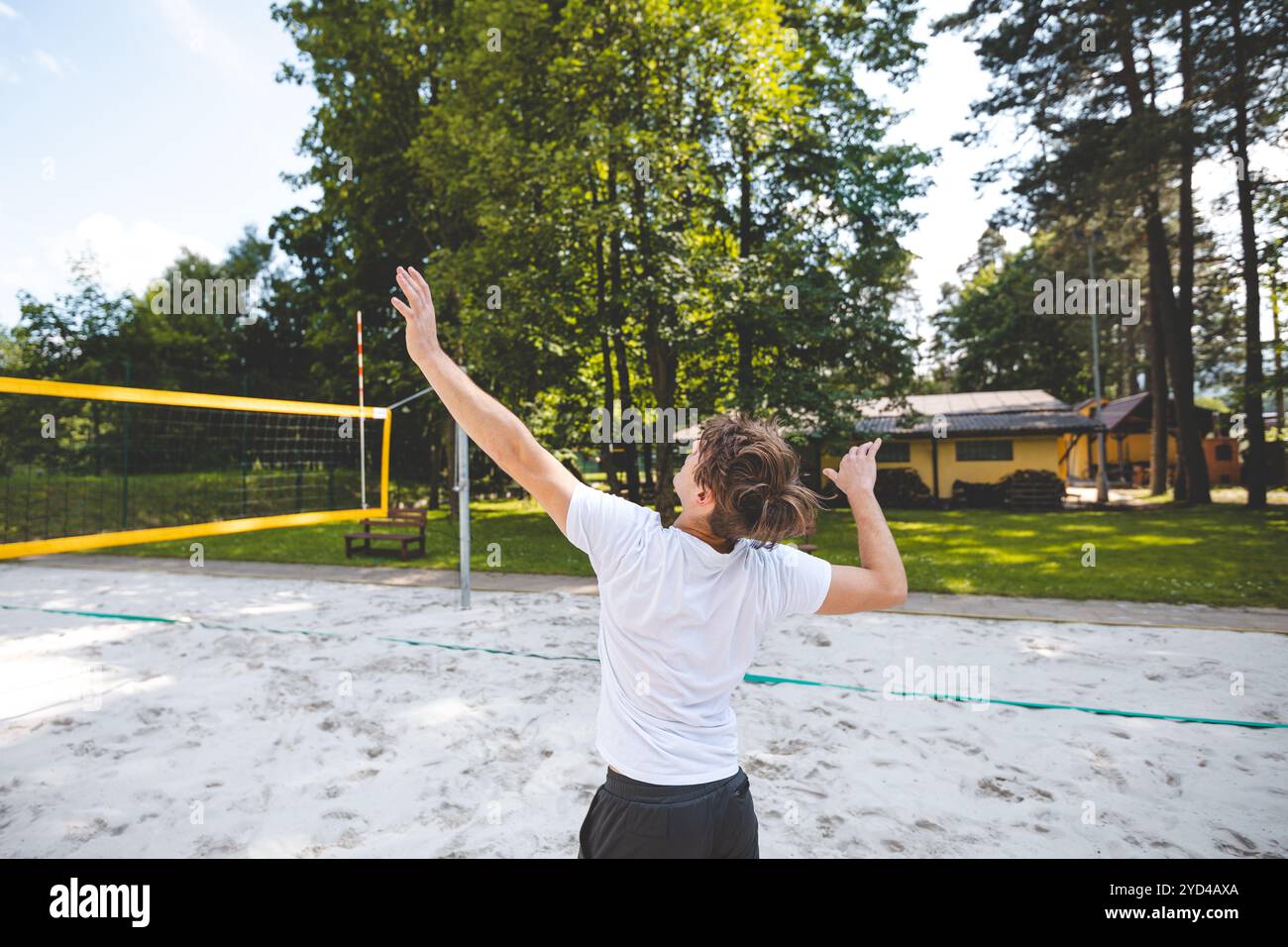 Volleyball player jumping to hit the ball over the net on a sand court ...