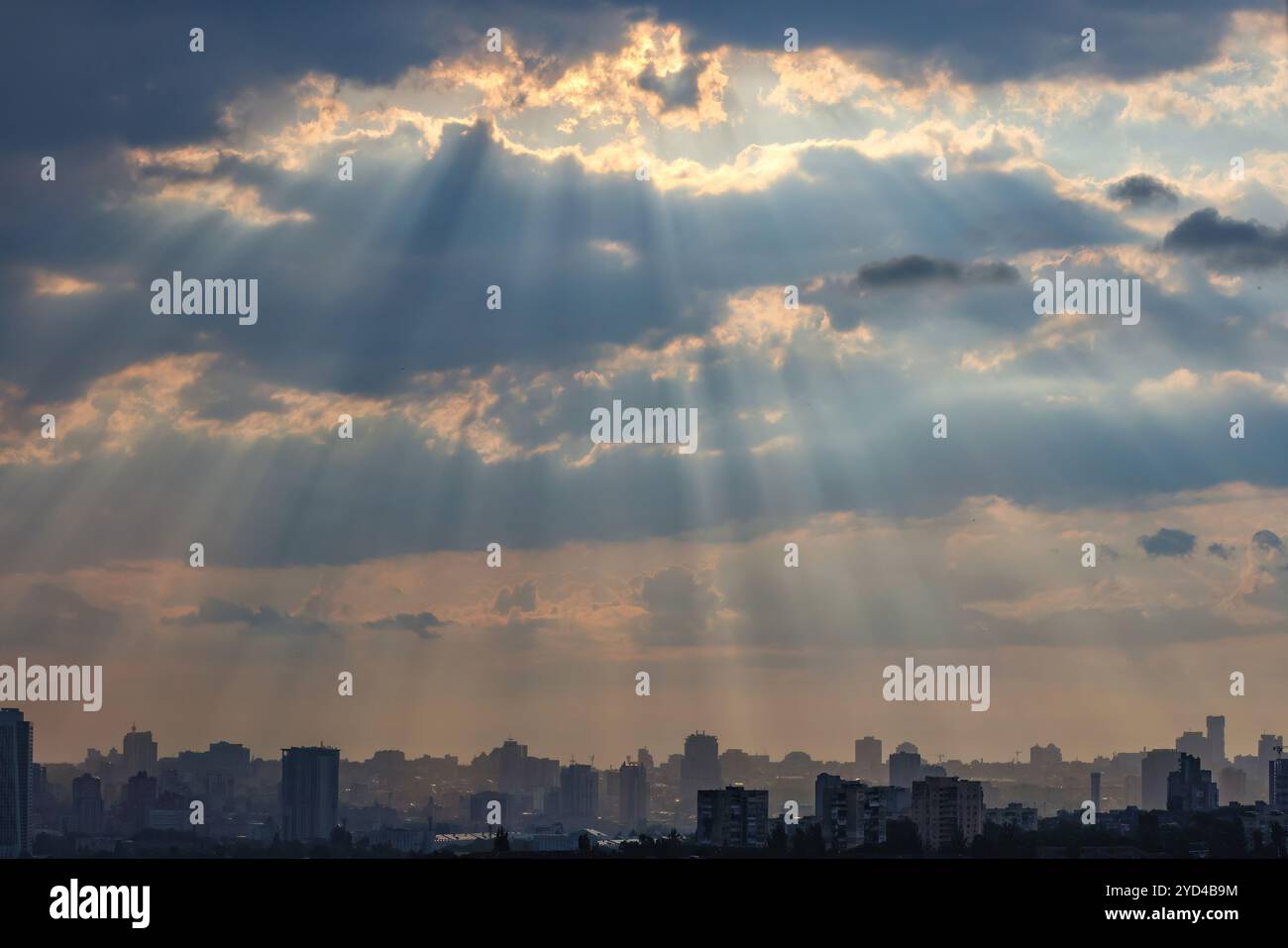 Dawn sun rays break through thick clouds over the silhouettes of houses ...