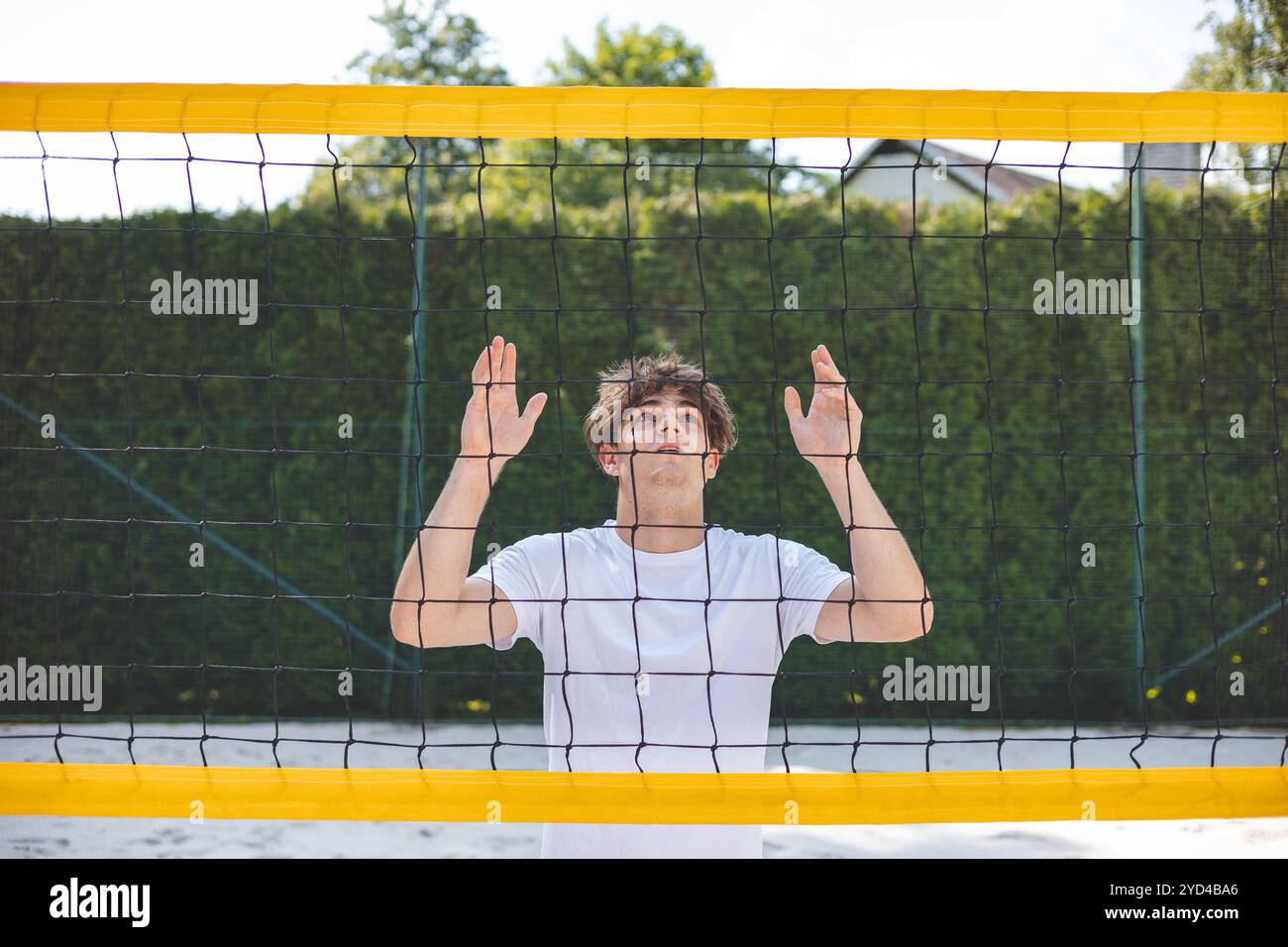 Volleyball player standing face-to-face with the net on a sand court ...