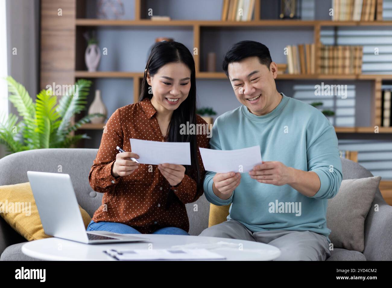 Asian couple happily reviewing documents at home with laptop. Image ...