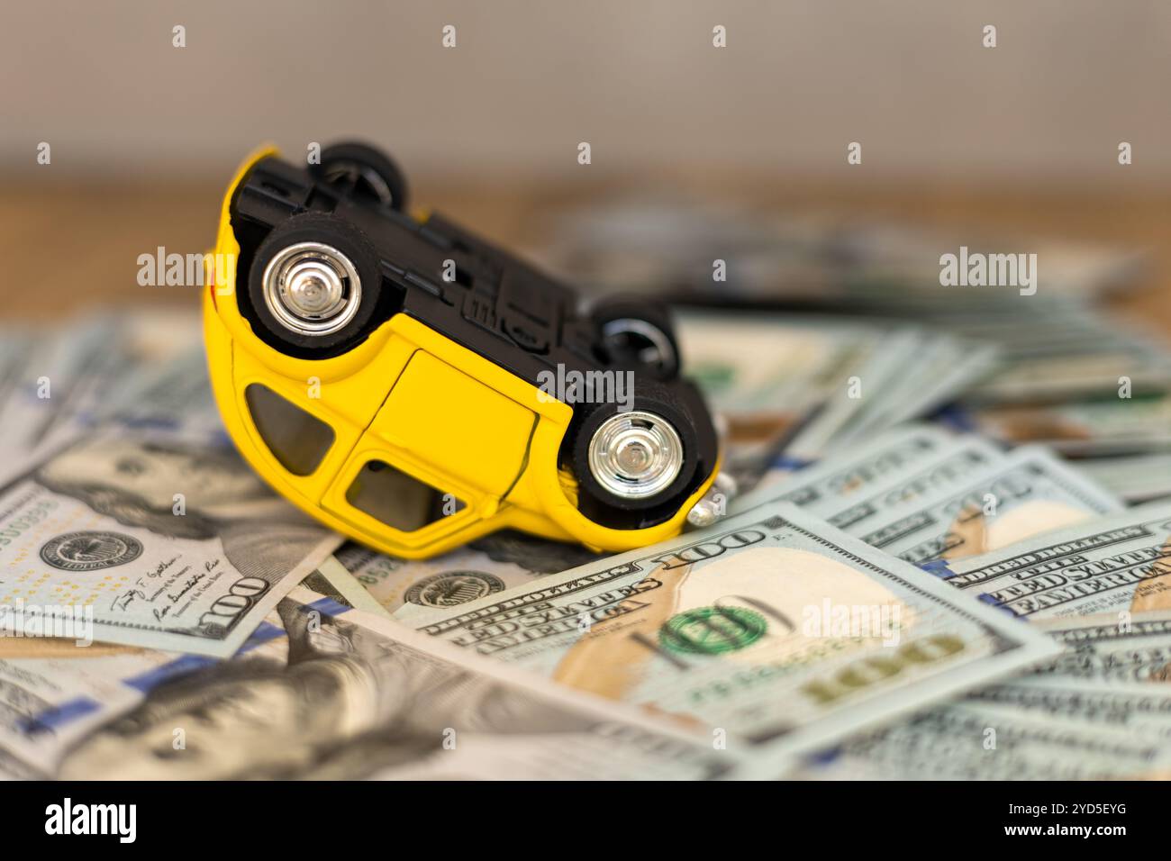 A toy yellow car upside down on a stack of hundred dollar bills in a creative financial display ...