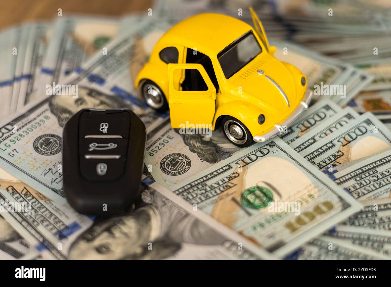A miniature yellow car with open doors placed on stacks of cash beside ...
