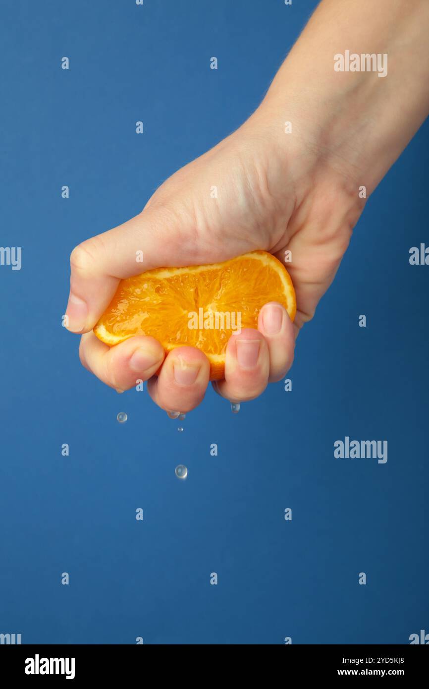Female hand squeezing half of orange on blue background. Top view Stock ...