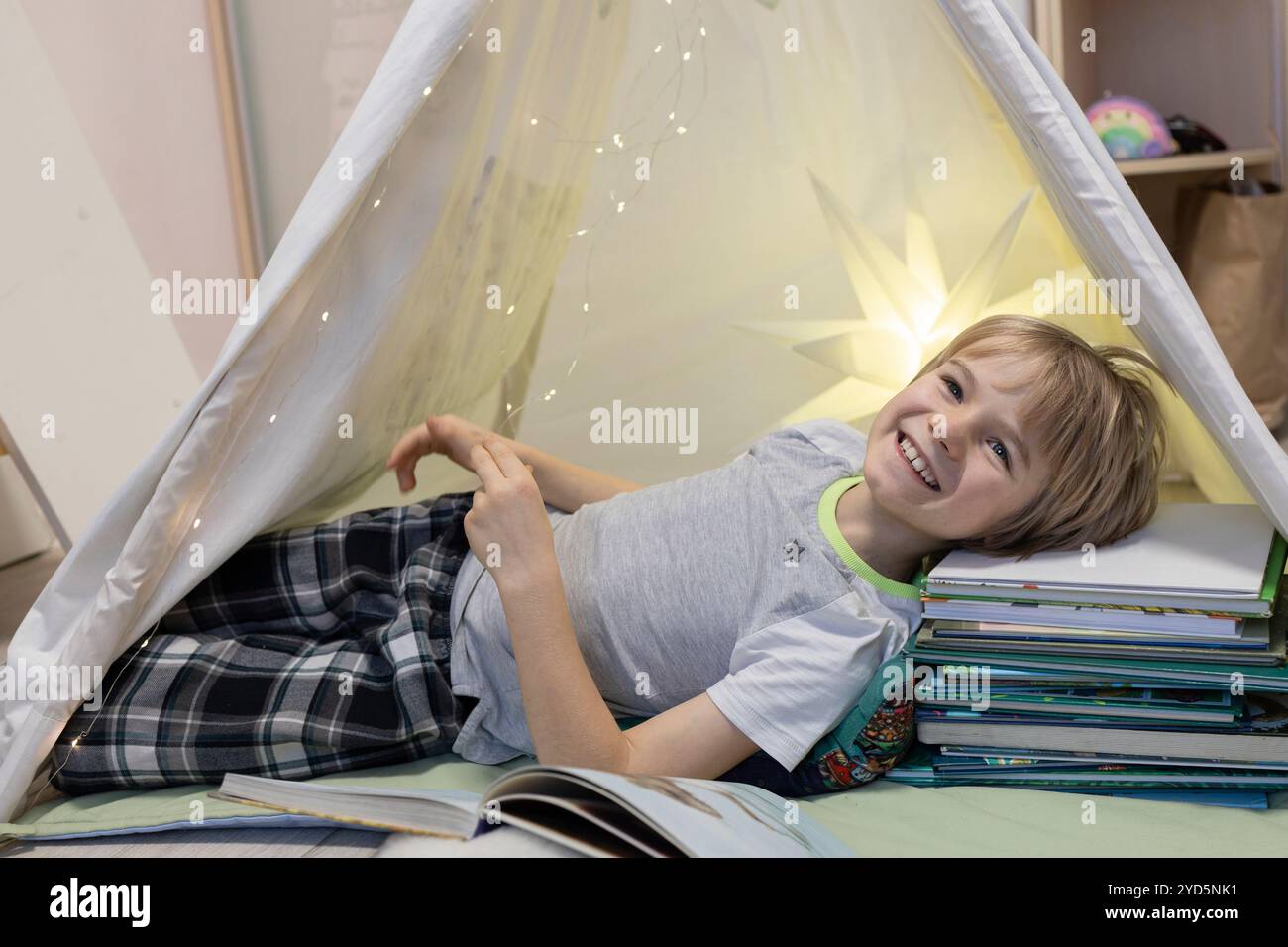 Cute 7 year old boy lies with his head on stacks of books in children's ...