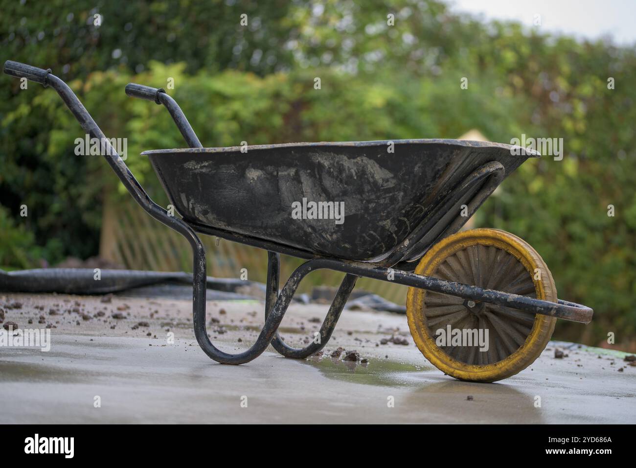 A sturdy, used wheelbarrow with a single yellow wheel stands outdoors ...
