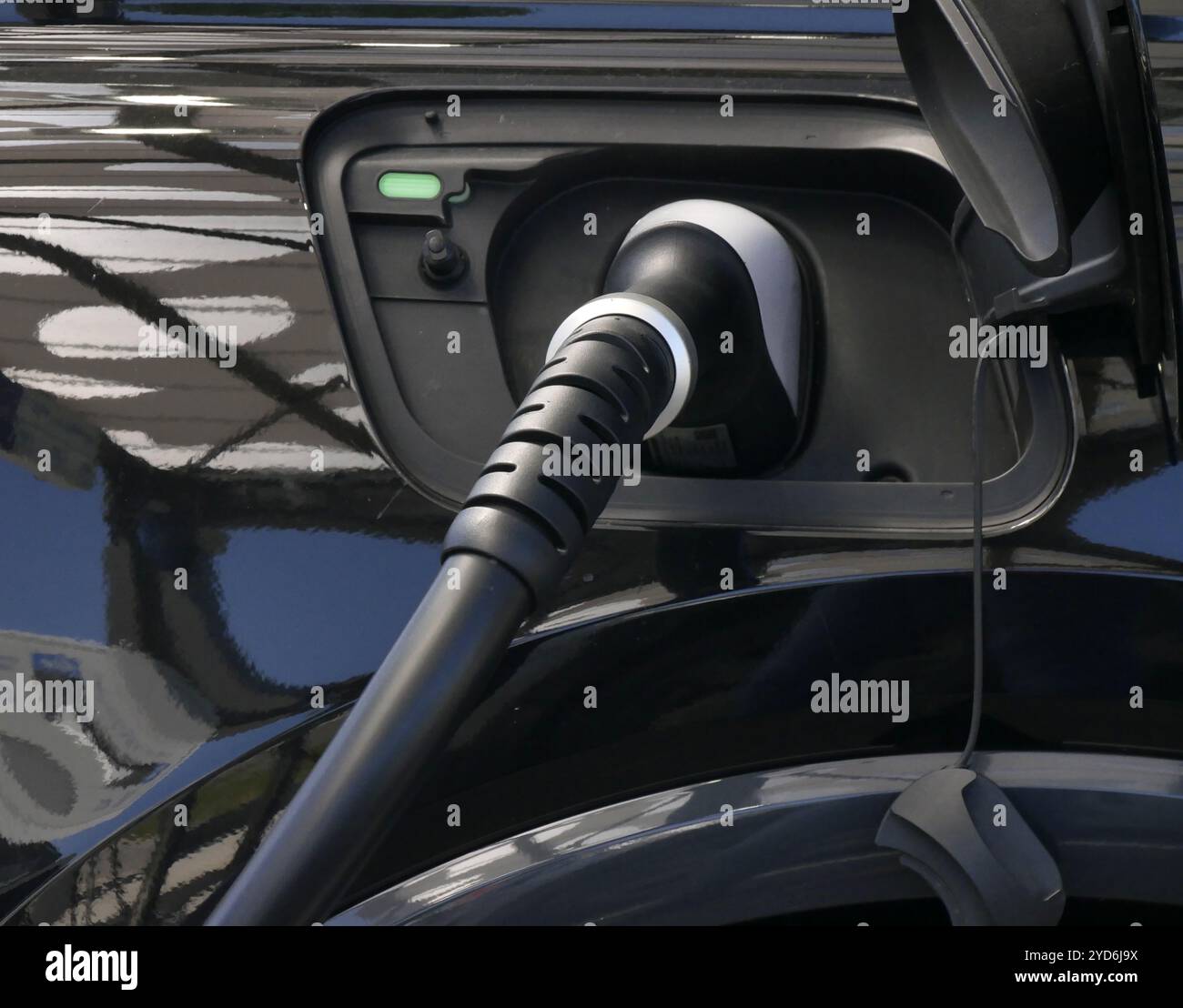 electric black car plugged to charge battery, close up of the plug ...