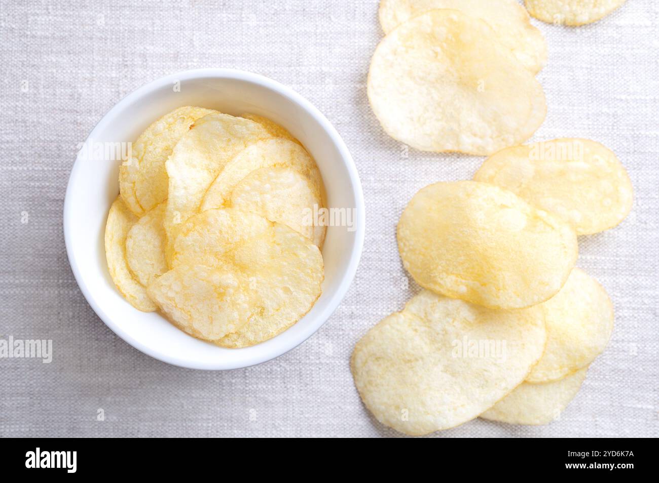 Salted potato chips in a white bowl on linen fabric. Fresh and ready to ...