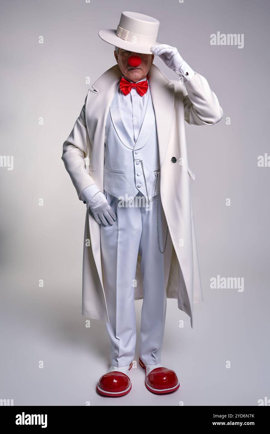 Serious mafia-like clown in a white coat, hat and large red patent ...