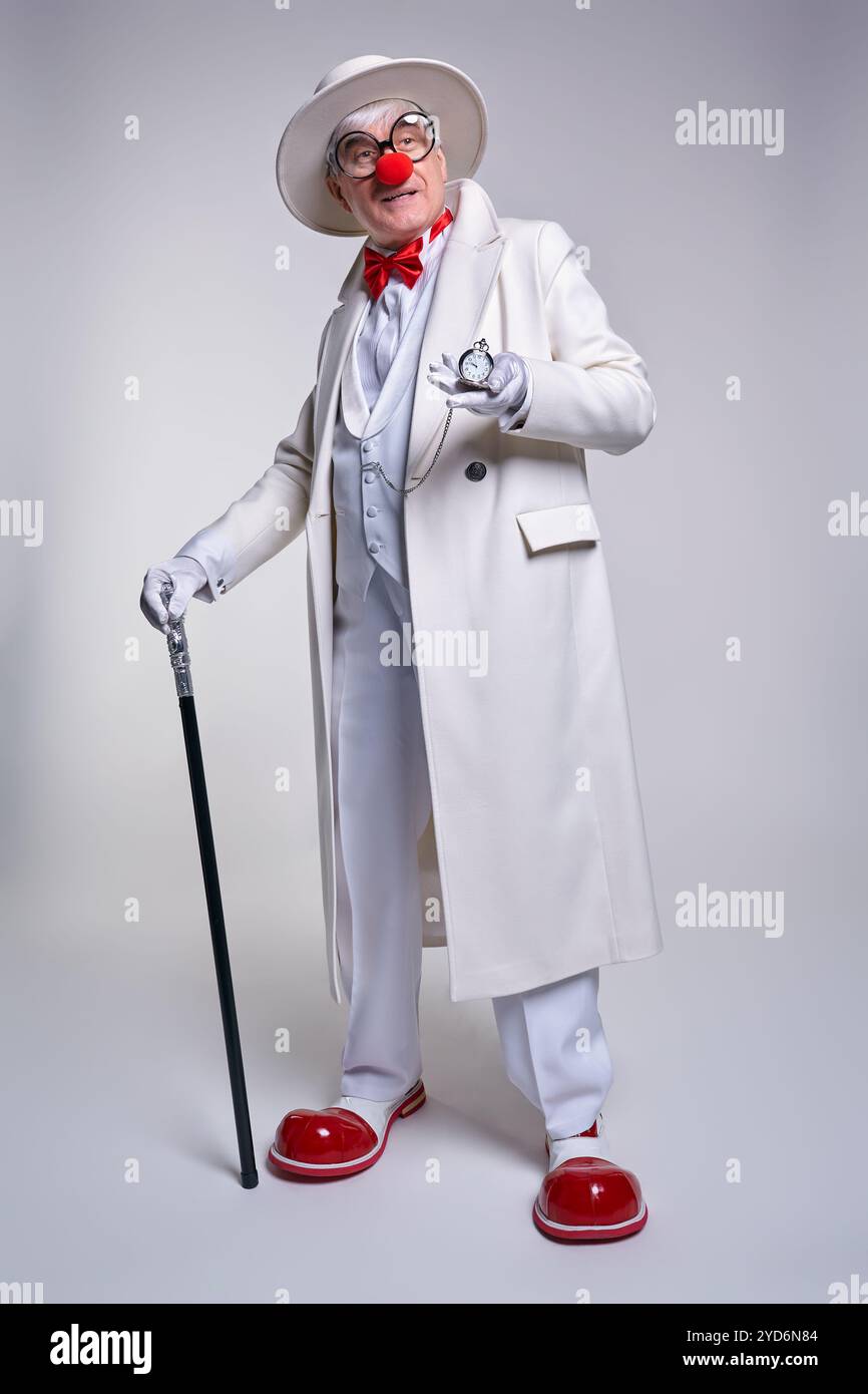 An elderly clown with an antique watch on a chain in his hand. Dressed ...