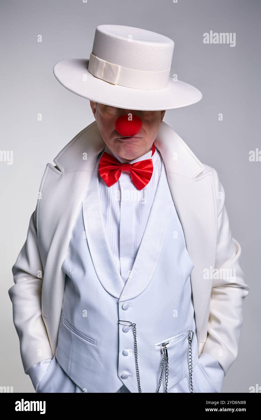 An elderly serious mafia-like clown in a white coat and hat. Hands in ...